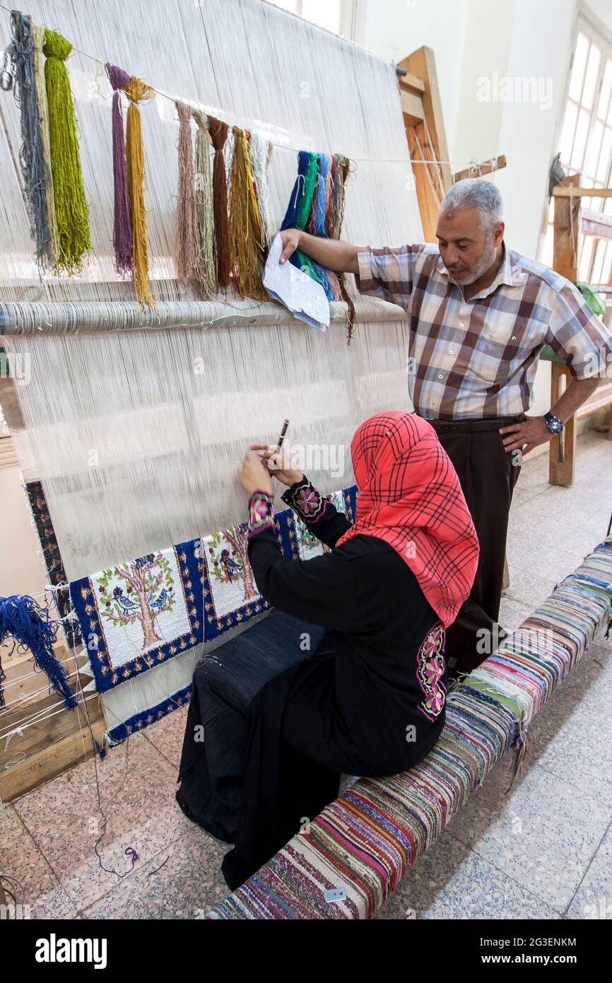 A factory manager oversees a lady weaving a hand-made carpet on a loom at a factory at Cairo in ...