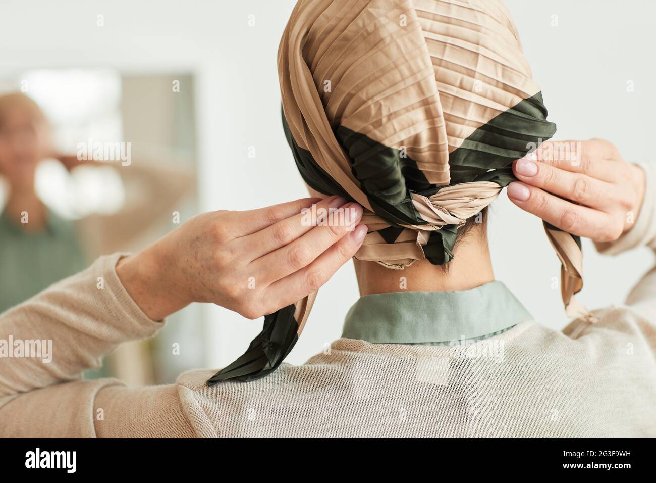 Back view at mature woman putting on headscarf by mirror and getting ...
