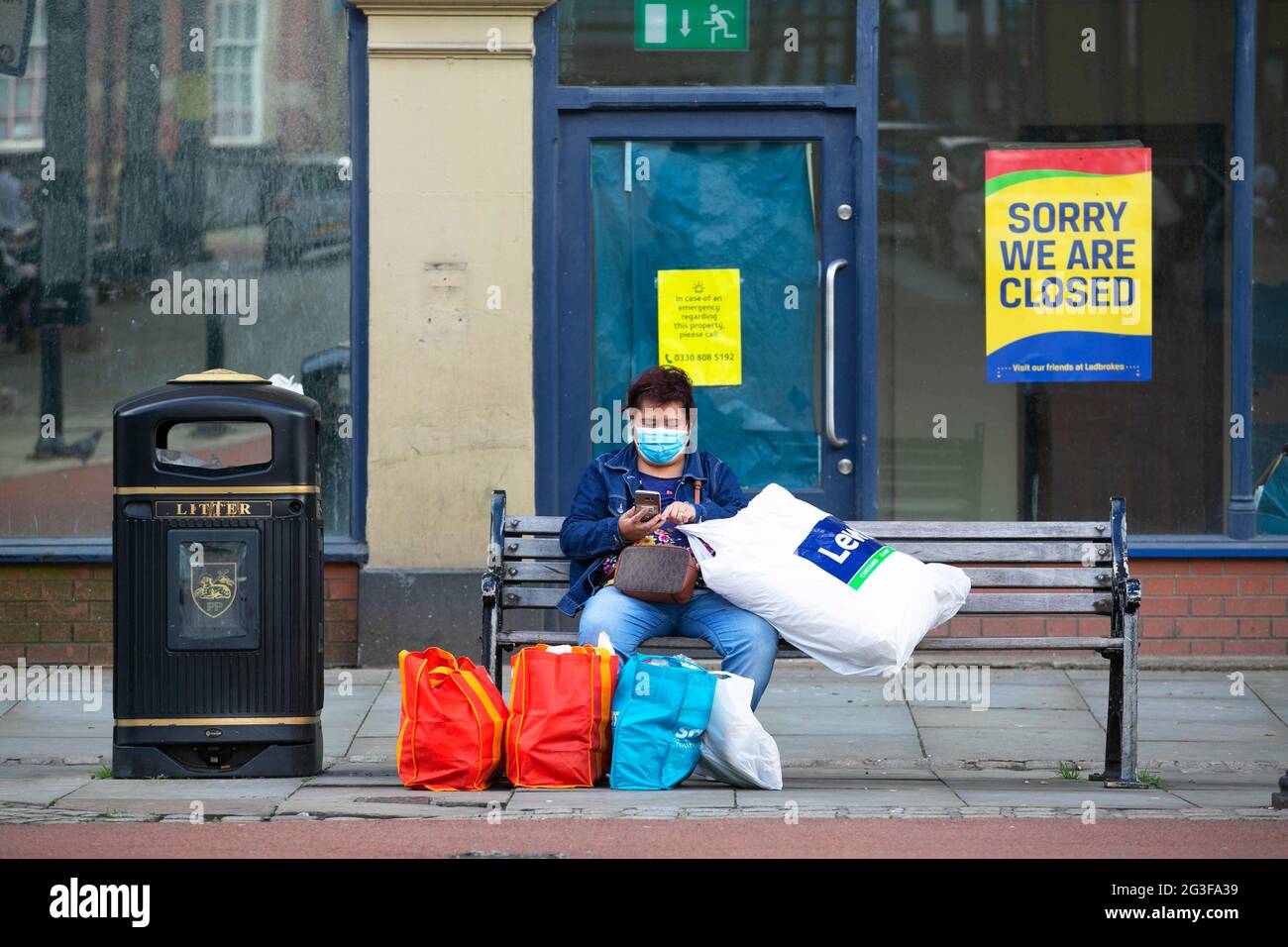 A woman in a face mask sits with shopping bags infront of a closed shop ...