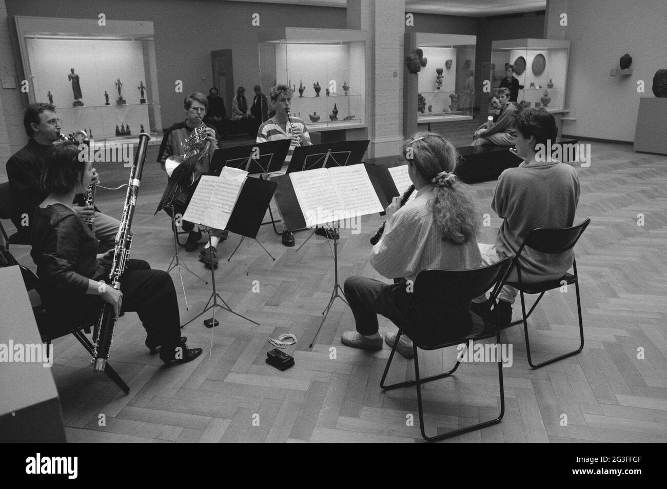 Seated musicians play bladder instruments in a room with showcases ...