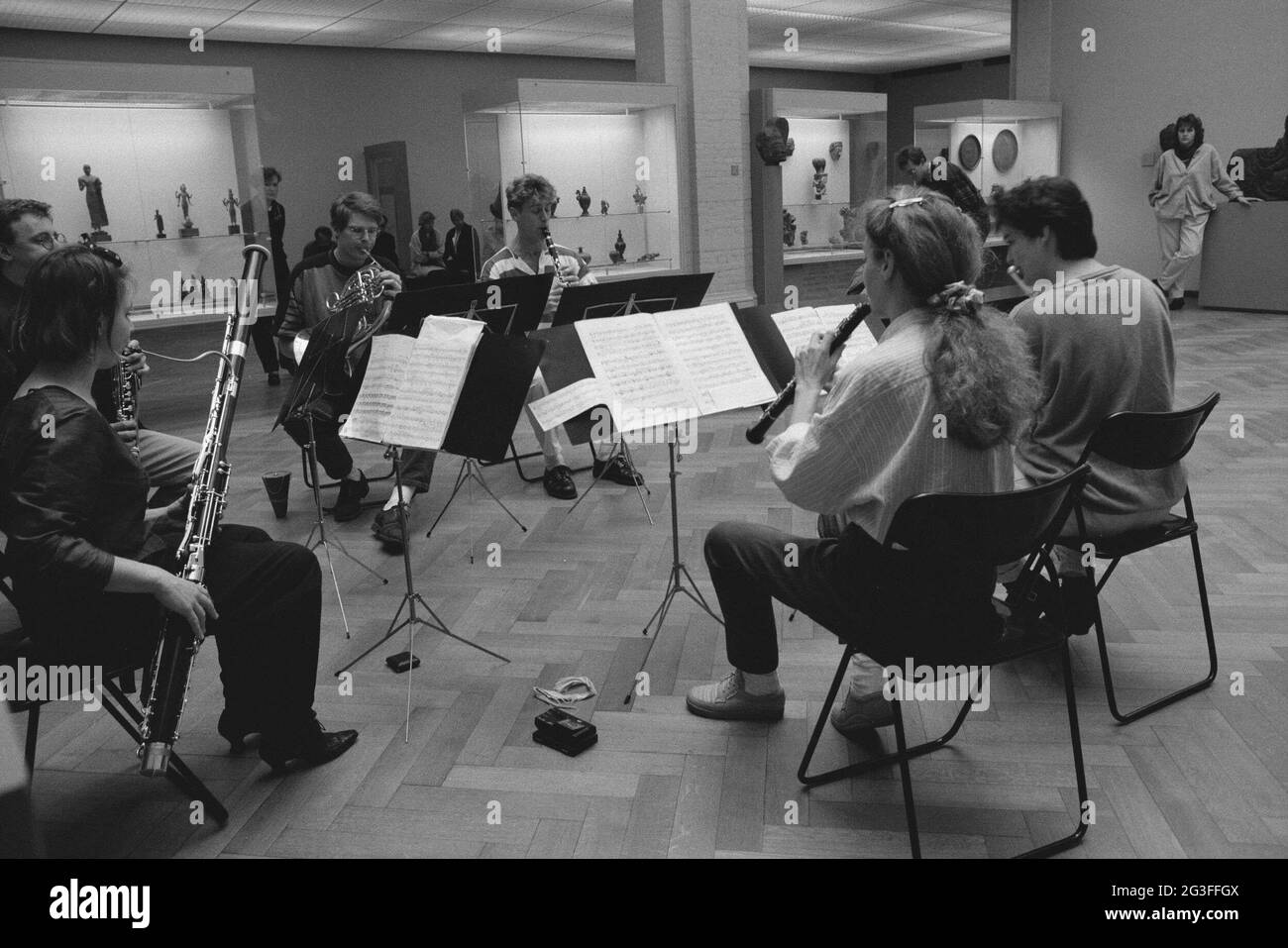 Seated musicians play bladder instruments in a room with showcases ...