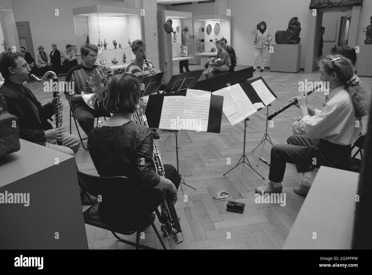 Seated musicians play bladder instruments in a room with showcases ...