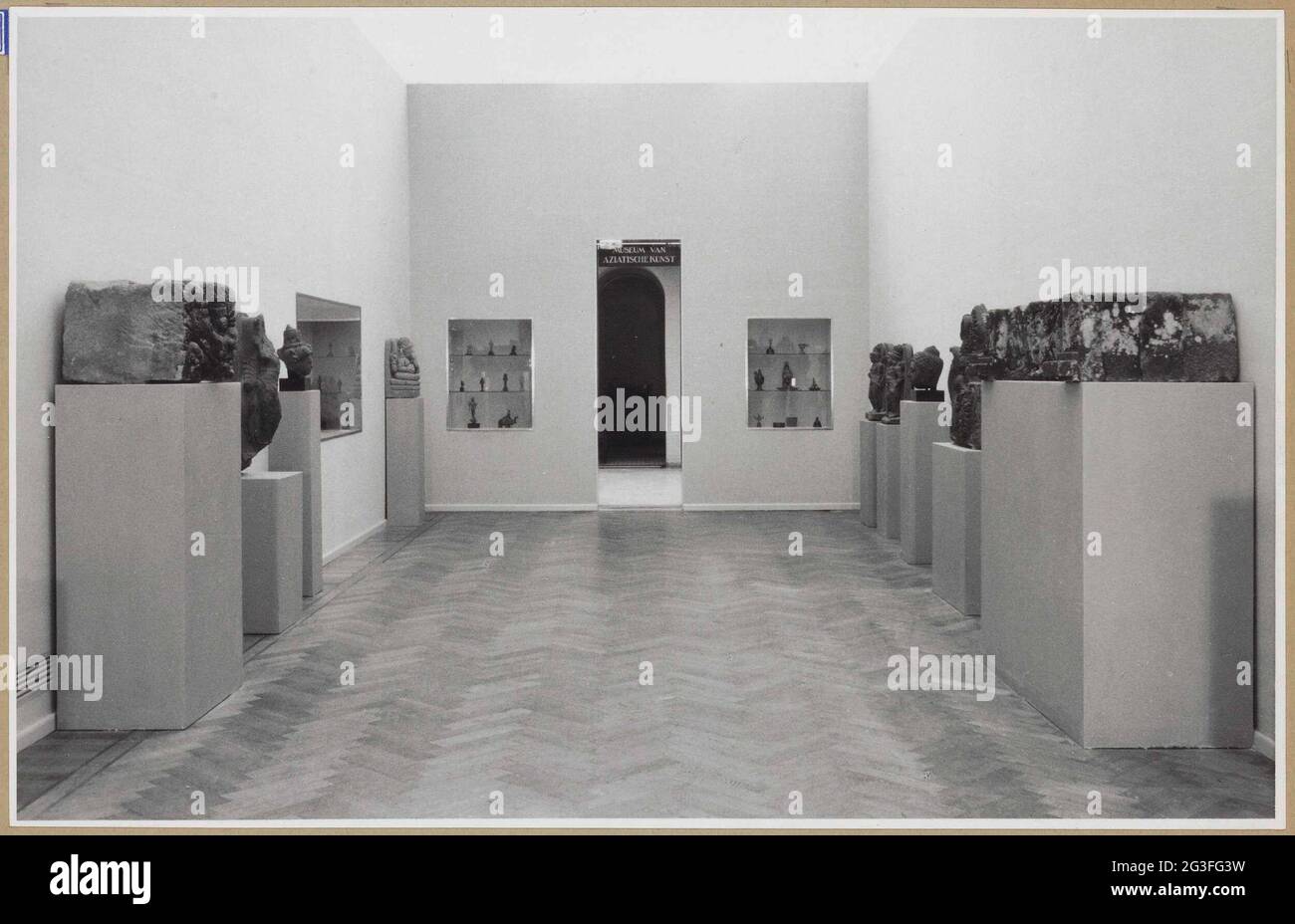 Room with sculptures on pedestals and three built-in showcases, a passage at the back; Asian art ...