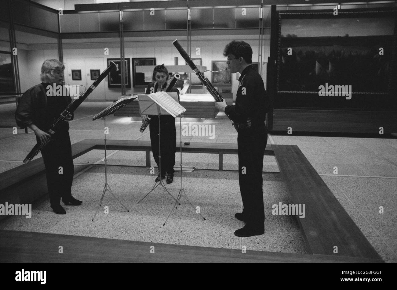 Two standing women and a man playing bladder instruments in a square ...