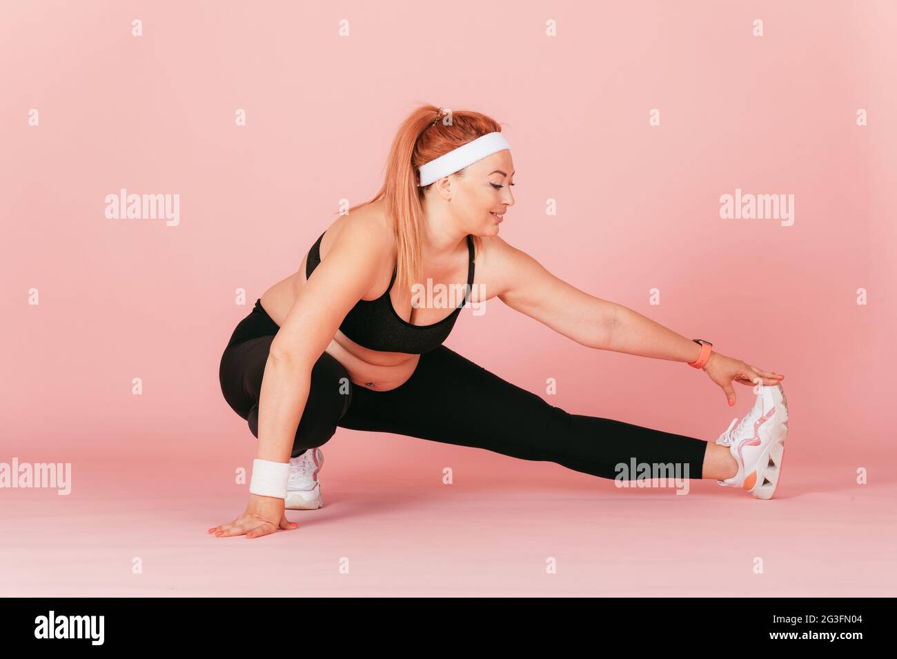 Happy young woman with plus size body wearing sport outfit doing leg ...