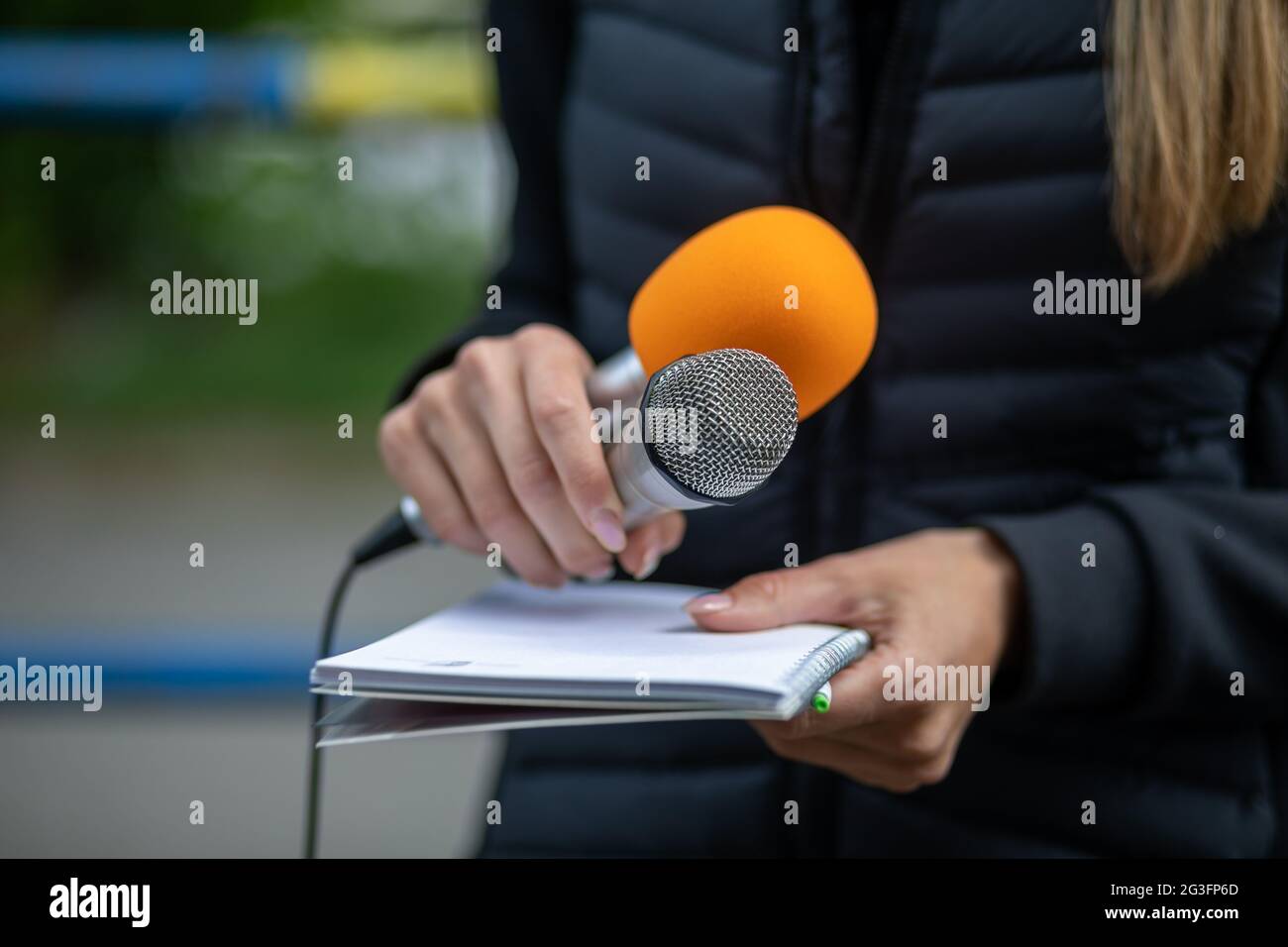 Female journalist at news conference, writing notes, holding microphone ...