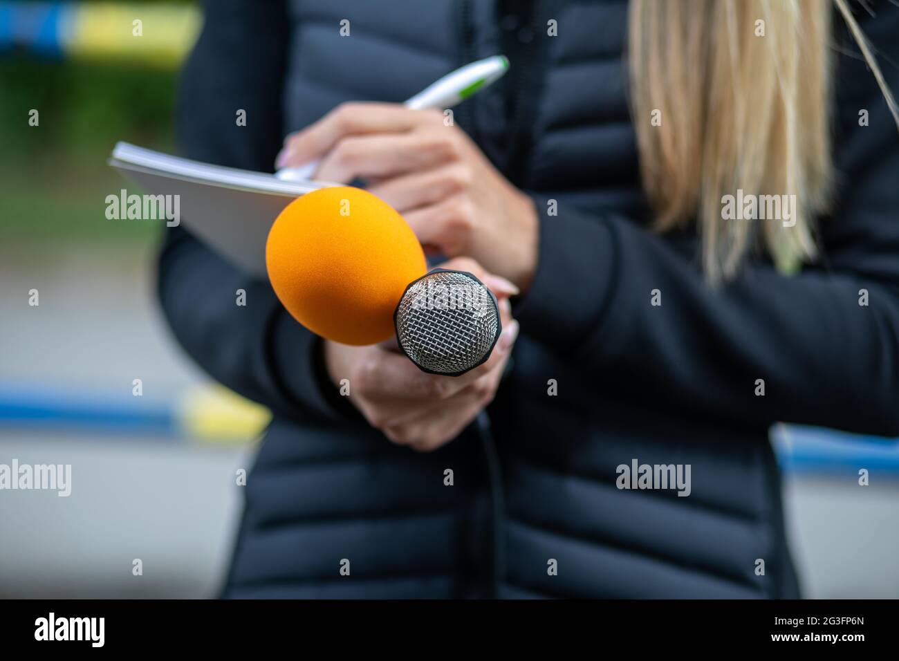 Female journalist at news conference, writing notes, holding microphone ...