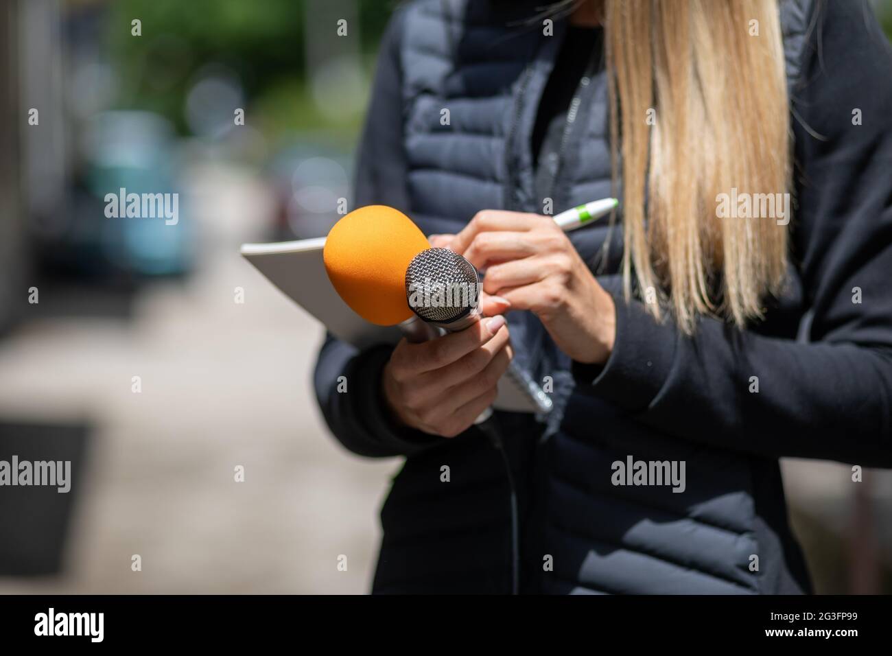 Female journalist at news conference, writing notes, holding microphone ...