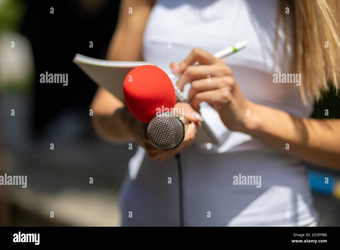 Female journalist at news conference, writing notes, holding microphone ...