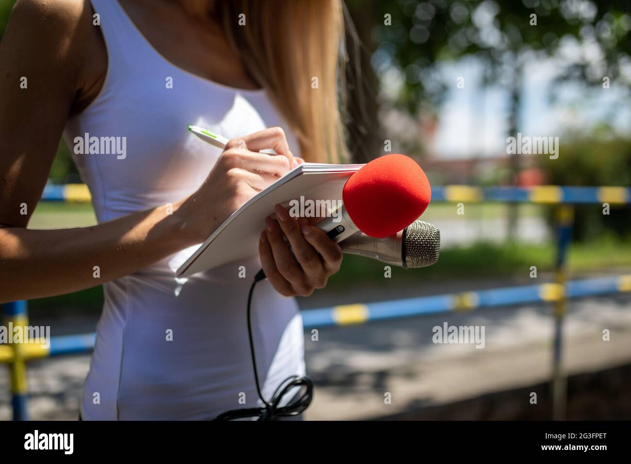 Female journalist at news conference, writing notes, holding microphone ...