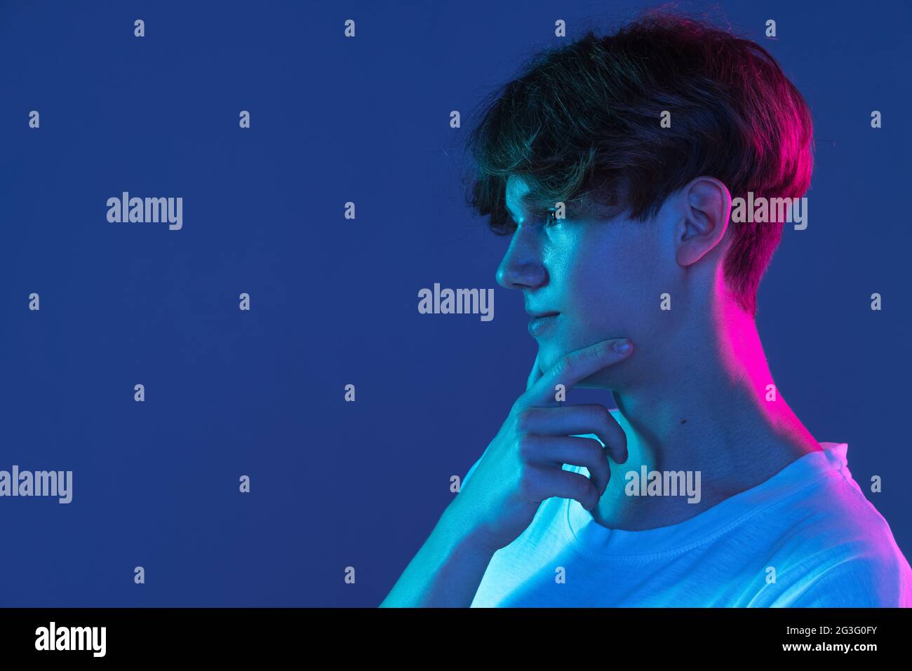 Caucasian young man's portrait on dark studio background in neon ...