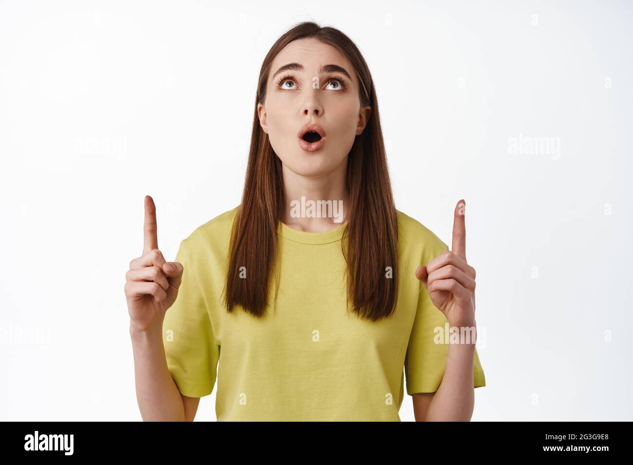 Portrait of amazed young woman pointing, looking up with excited face ...