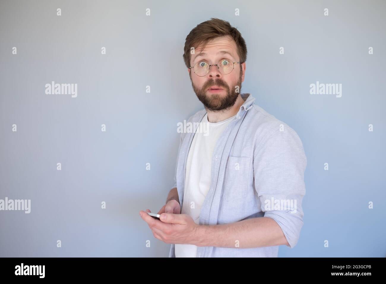 Confused, shocked man with a smartphone in hands looks at the camera in ...