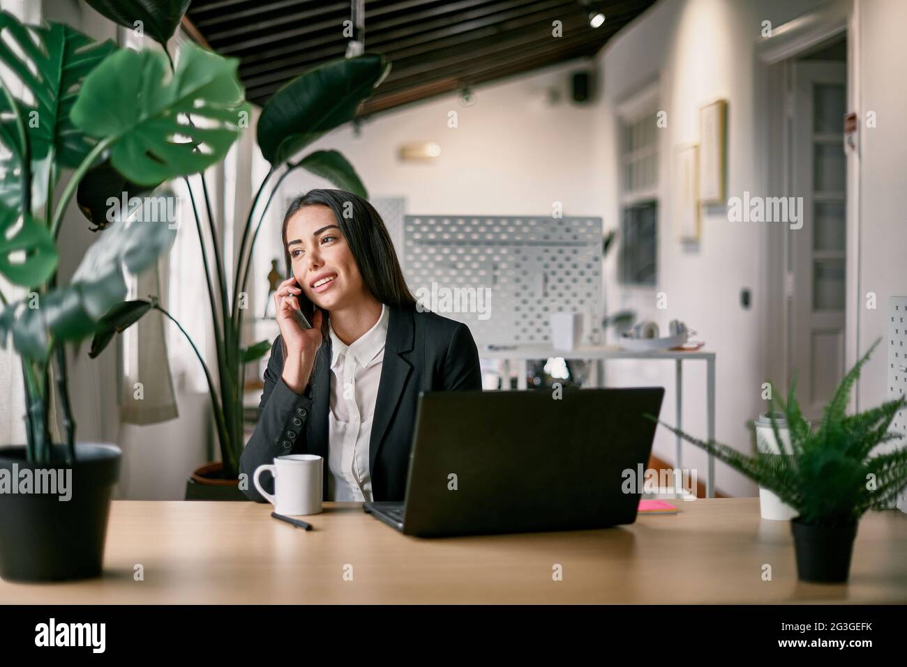 Smiling employee speaking on smartphone at desk with laptop Stock Photo ...
