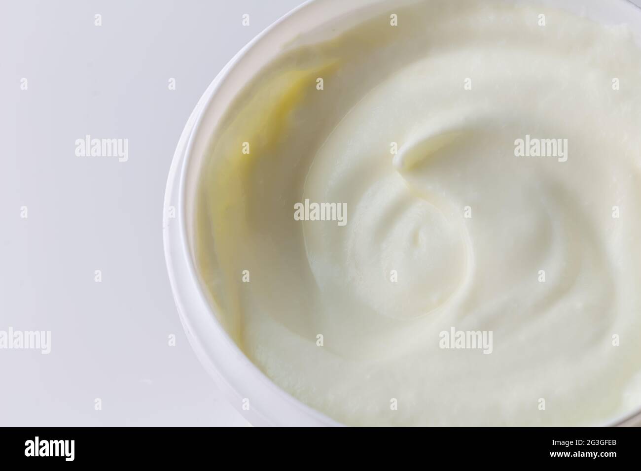 White yogurt in large plastic container close up on white with space ...