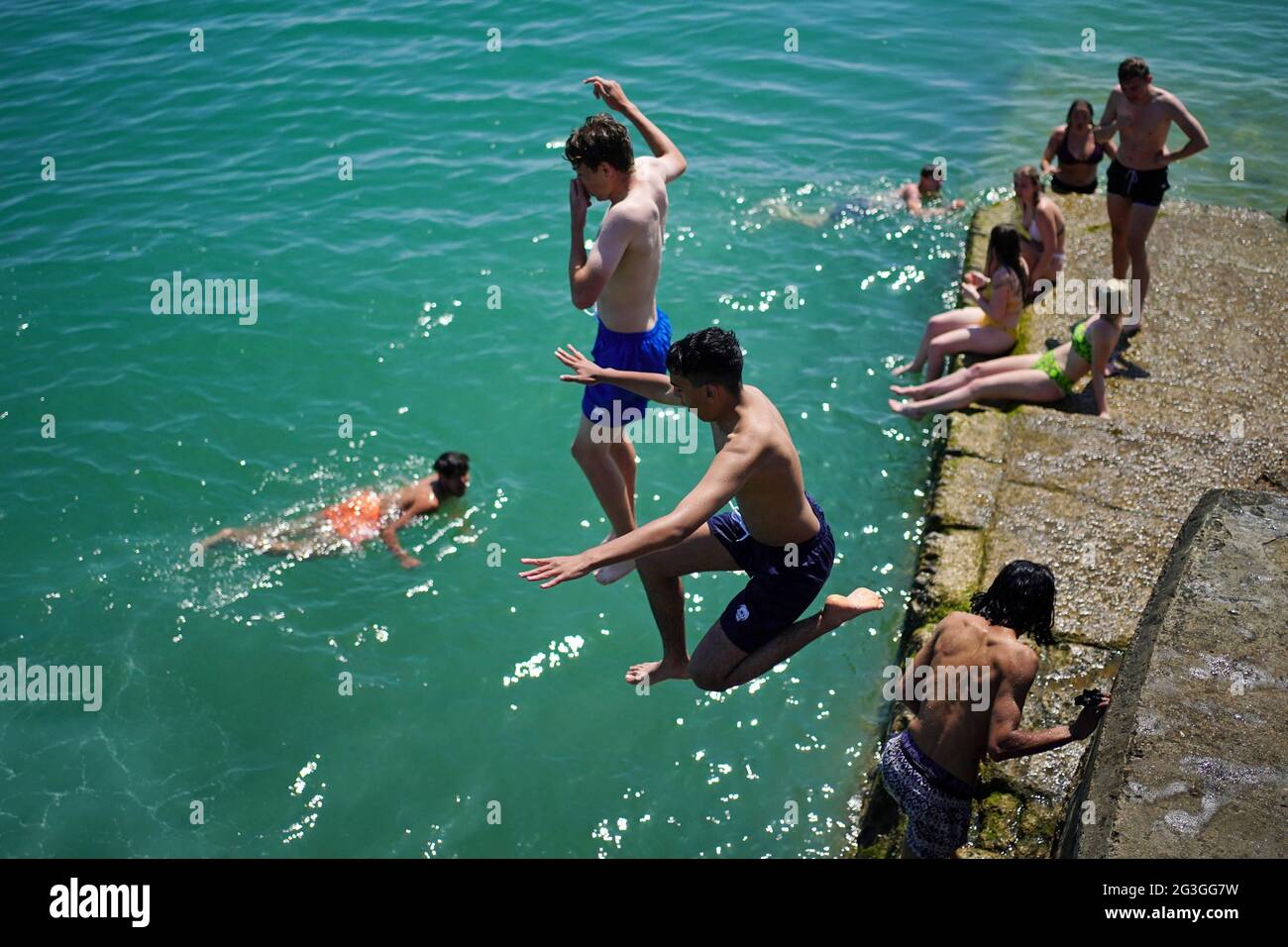 Two men dive into the sea whilst people enjoy the sunshine on Brighton ...