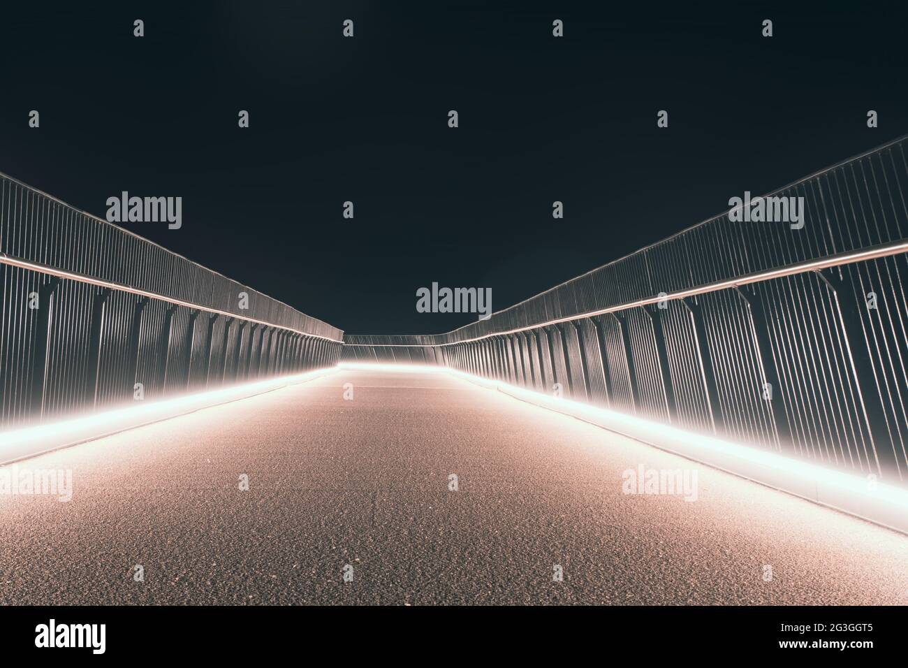 An empty modern footbridge, lit up by lights glowing on a summers night ...