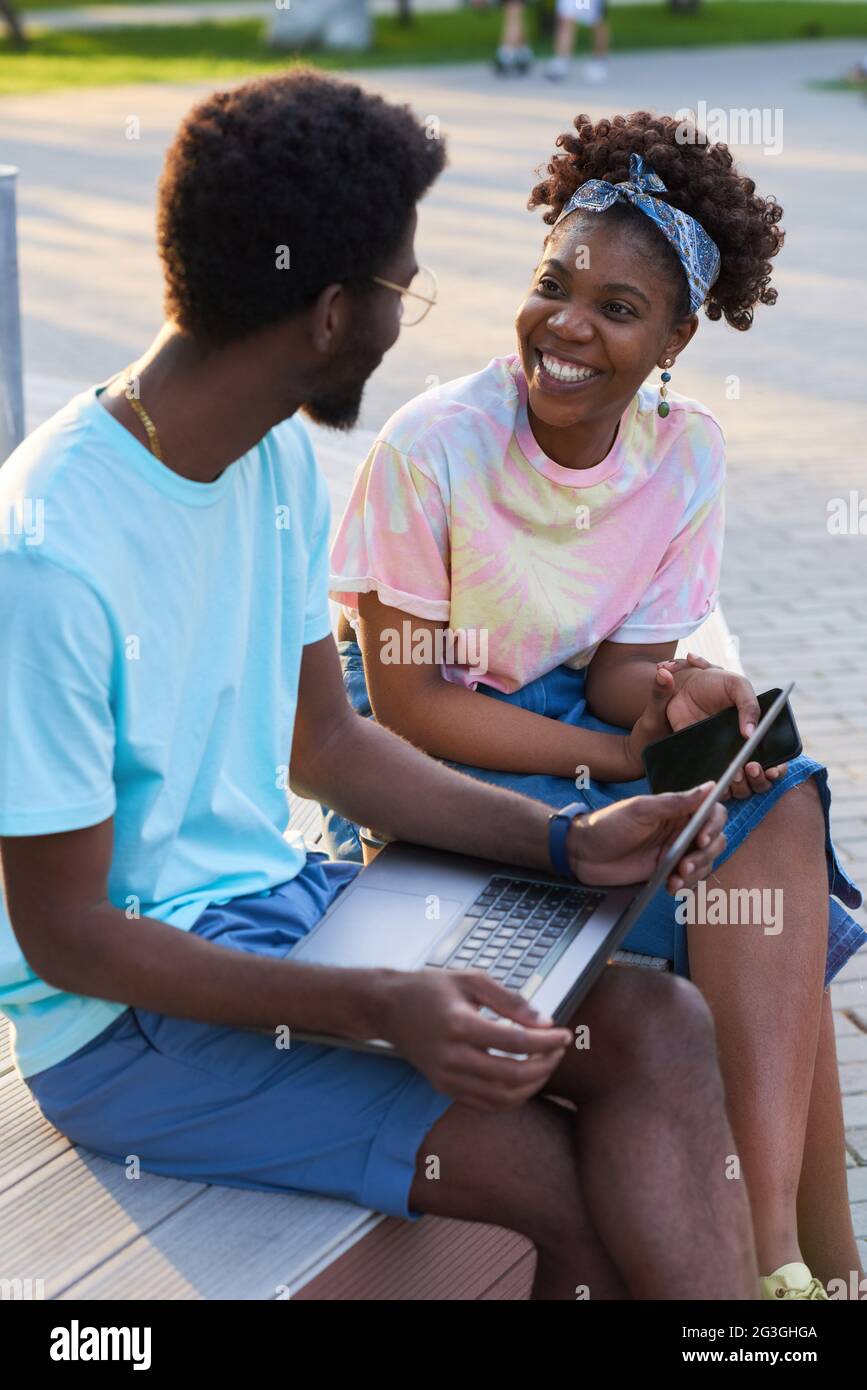 Happy African couple talking to each other and working on laptop ...