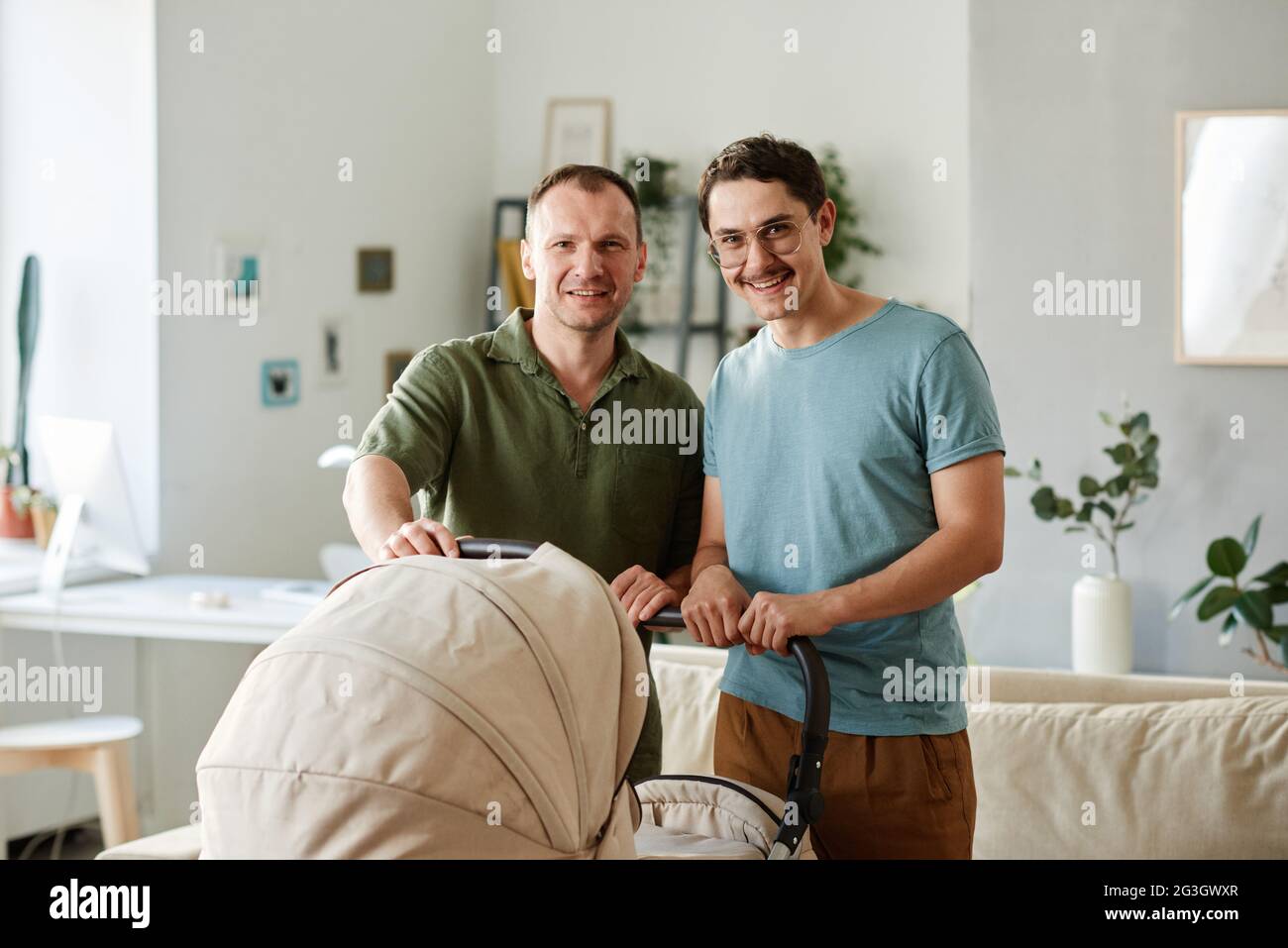 Portrait of happy gay family standing in the room with baby stroller ...