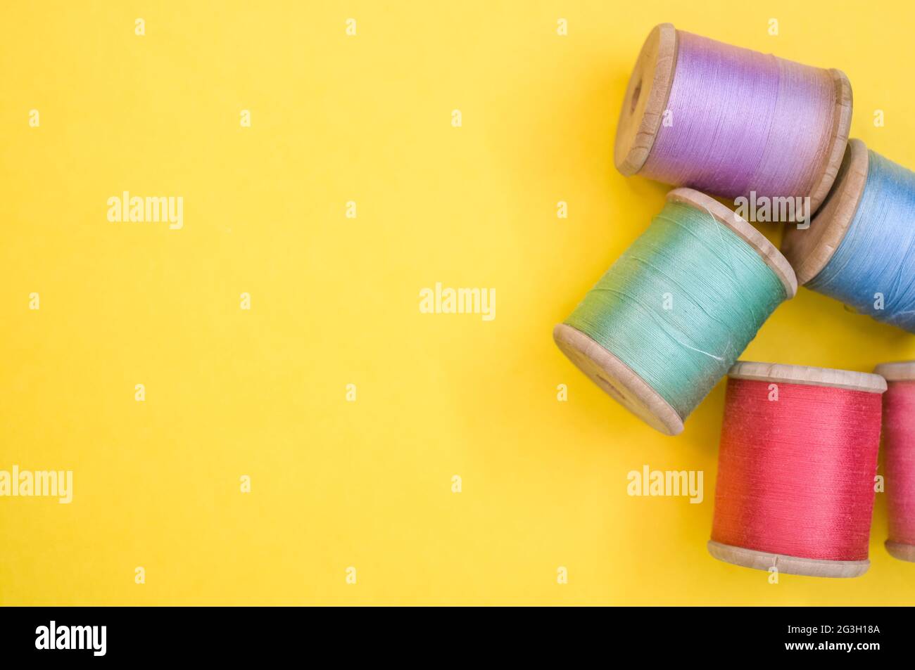 Colorful sewing threads isolated on a yellow background with free space ...