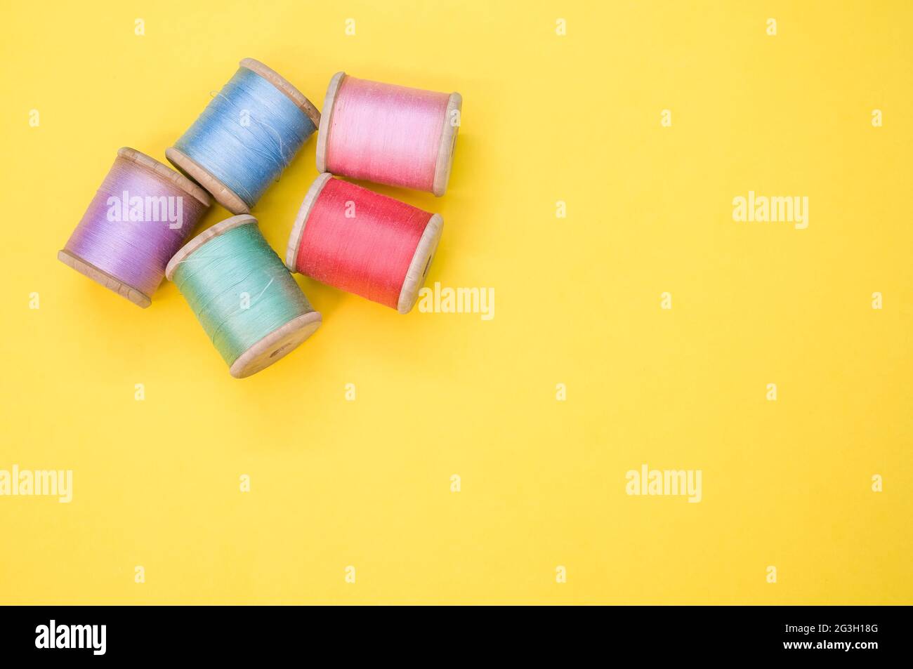 Colorful sewing threads isolated on a yellow background with free space ...