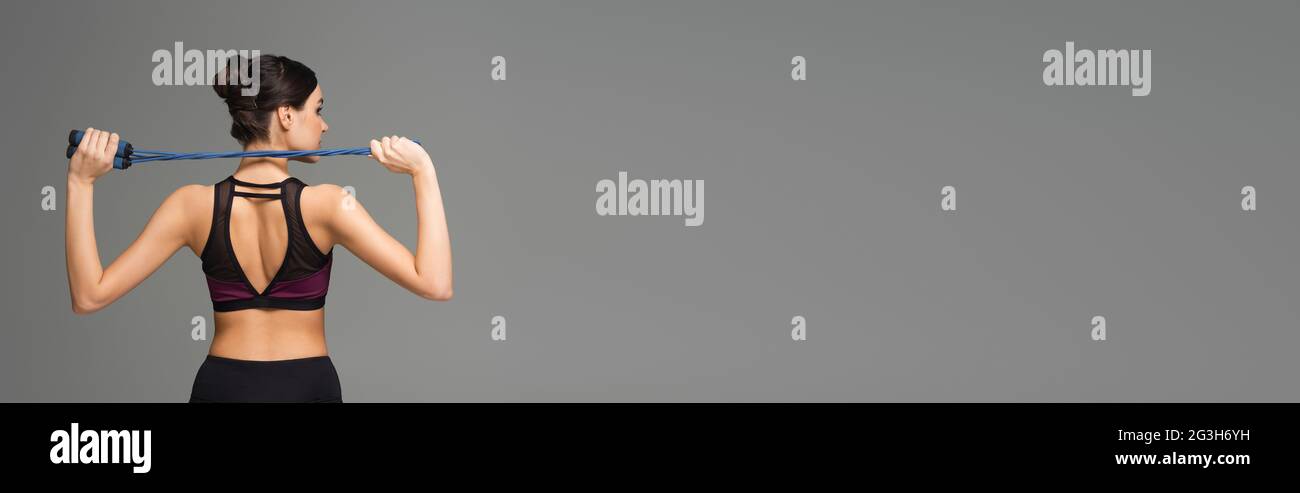back view of young woman in black sportswear holding jump rope isolated ...