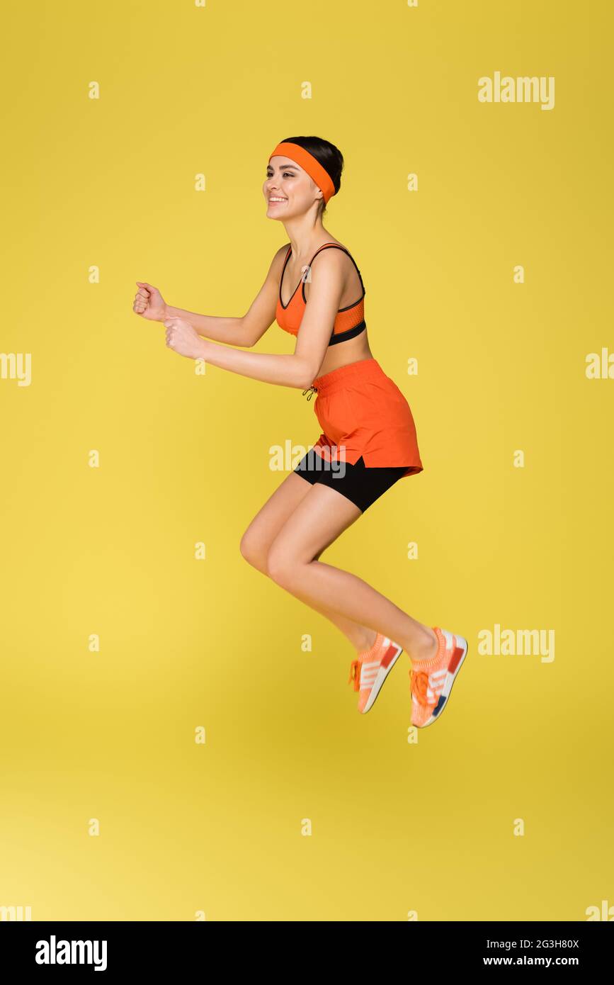 cheerful woman in orange sportswear jumping isolated on yellow Stock ...