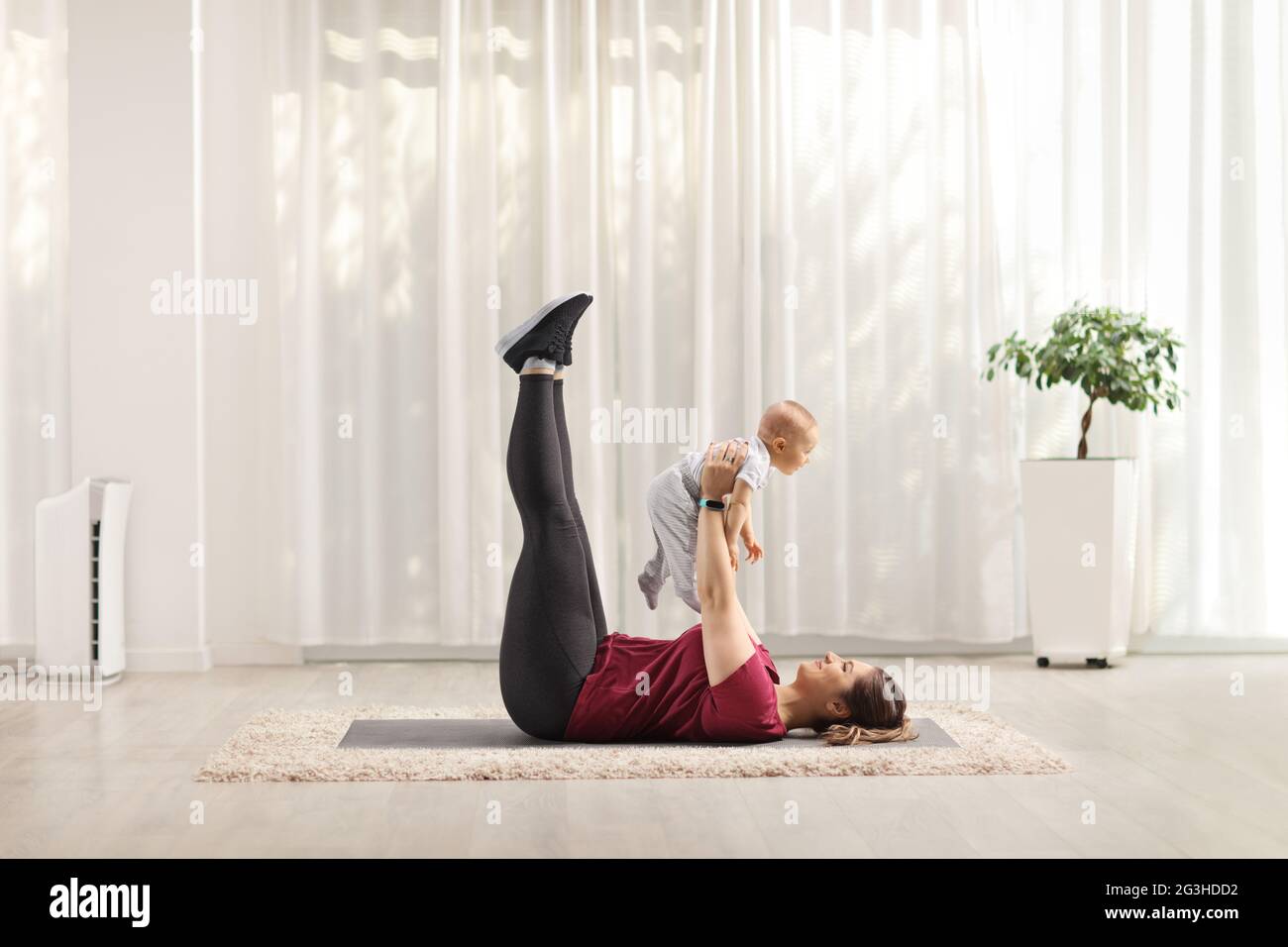 Mother on an exercise mat and lifting a baby at home in a living room ...