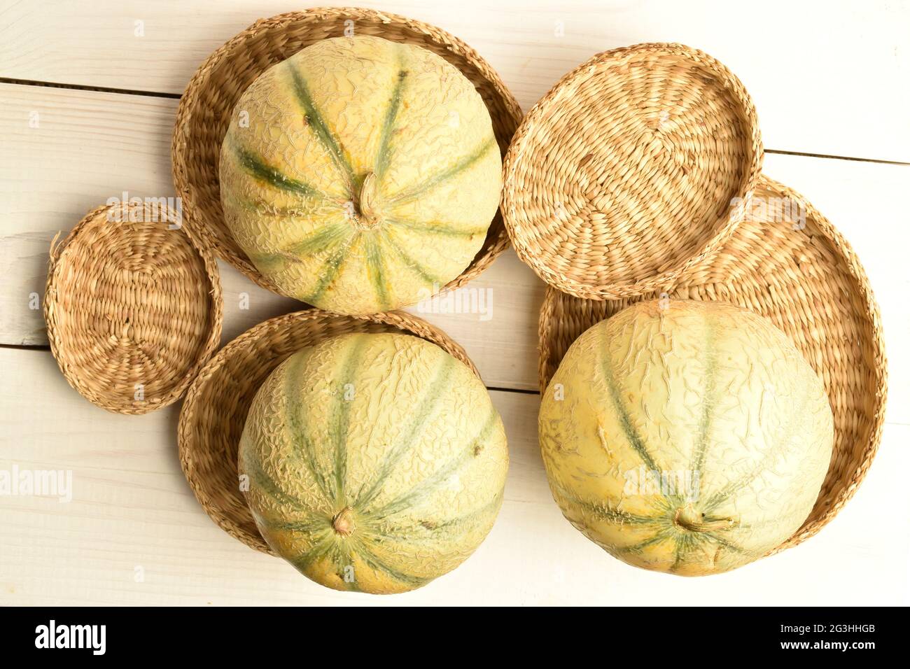 Three fragrant organic melons on straw plates, close-up, on a white ...