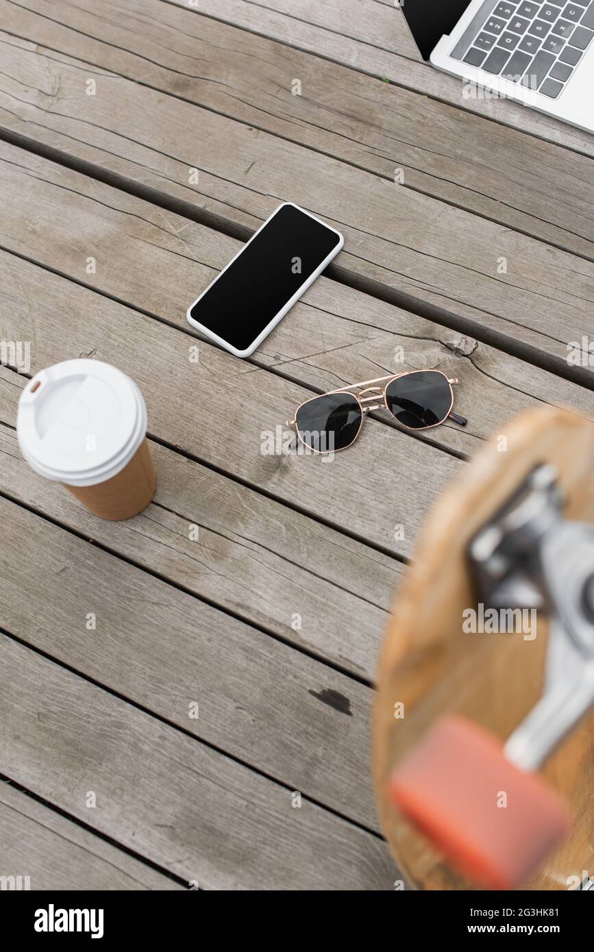high angle view of gadgets with blank screen, sunglasses and paper cup ...