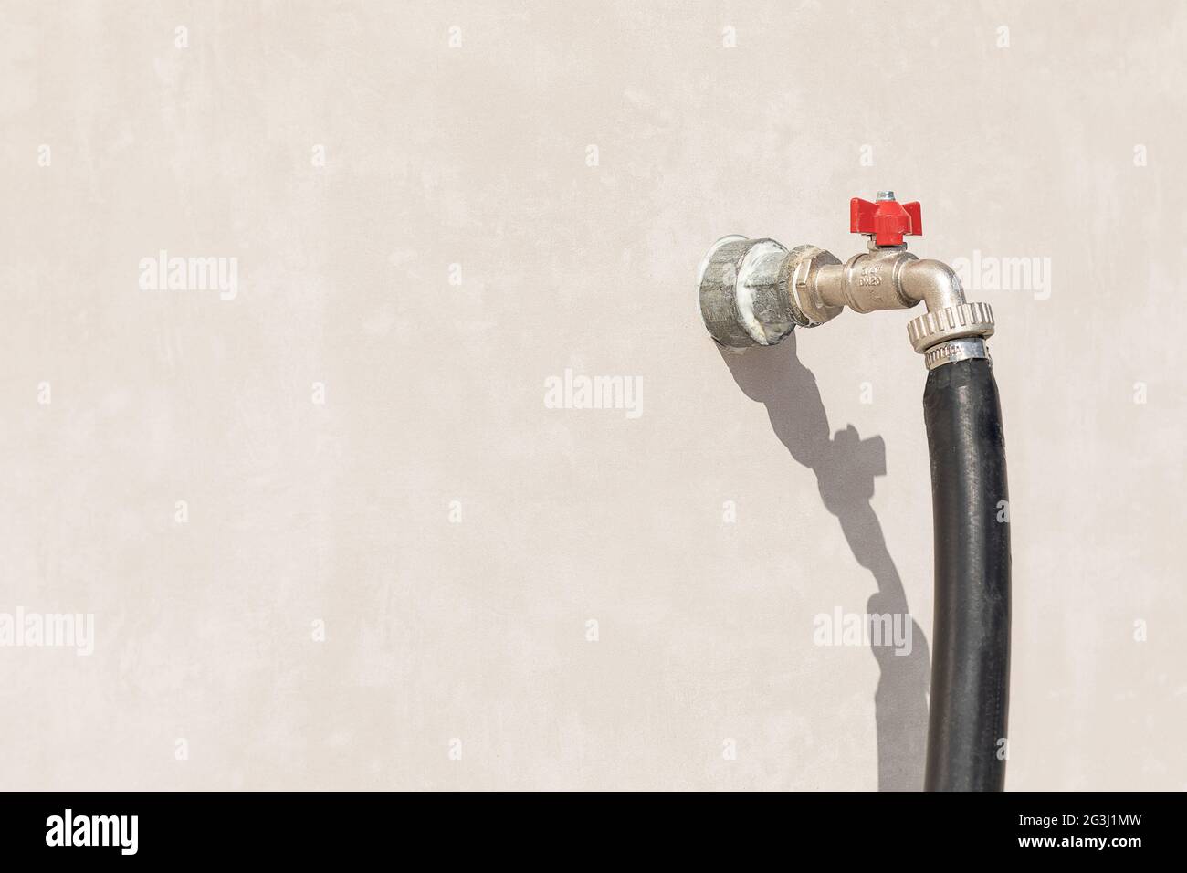 Water tap with red valve and hose, from outer, street wall of building ...
