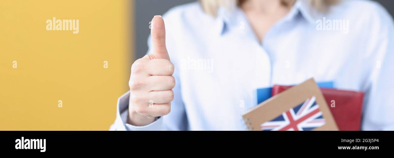 Woman holds textbooks with UK flag and shows thumbs up Stock Photo - Alamy
