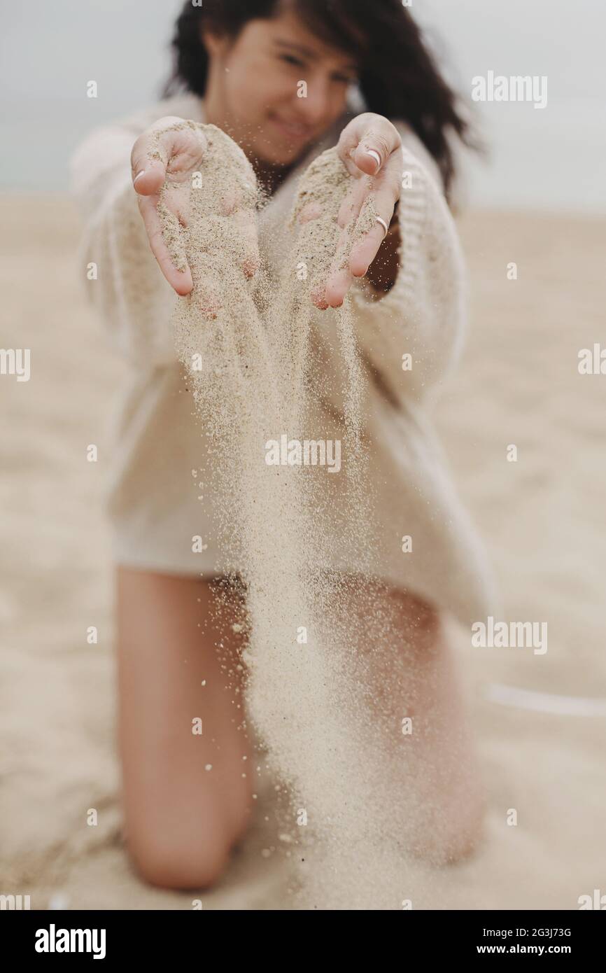 Stylish young woman in sweater releasing sand on beach, hands close up ...