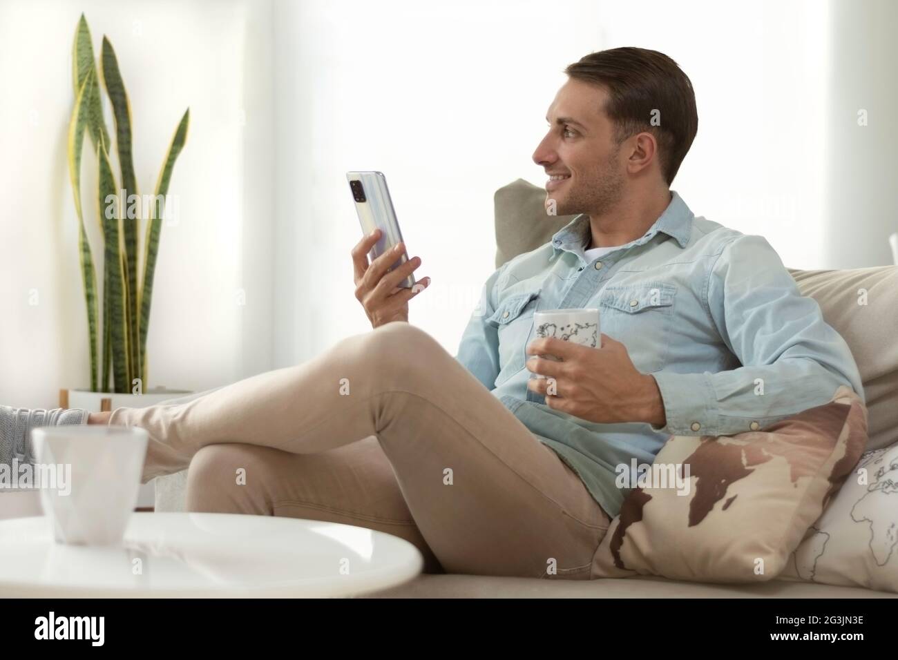 handsome young man, holding his smartphone, looking out the window ...