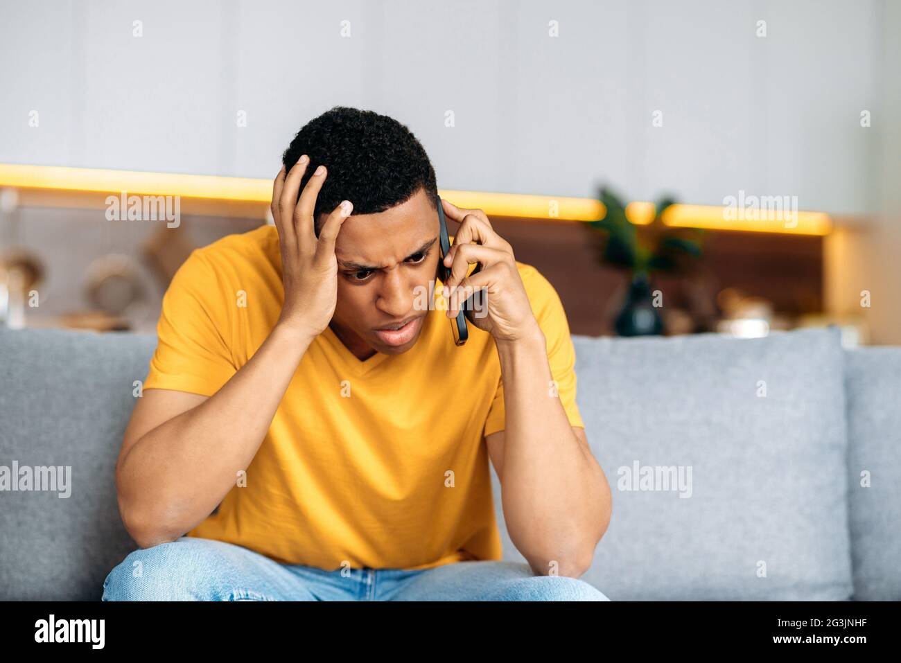 Confused sad latino guy sitting on a sofa in the living room, dressed ...