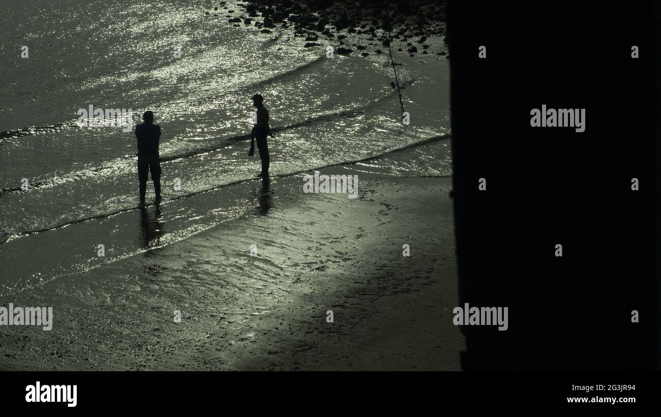 Silhouette of two men standing on a sandy beach, a sunny evening on the ...