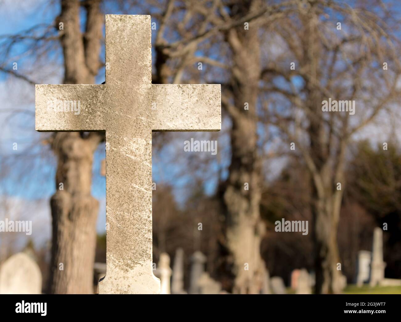 A dirty white stone cross in a graveyard. The cross is plain with no ...