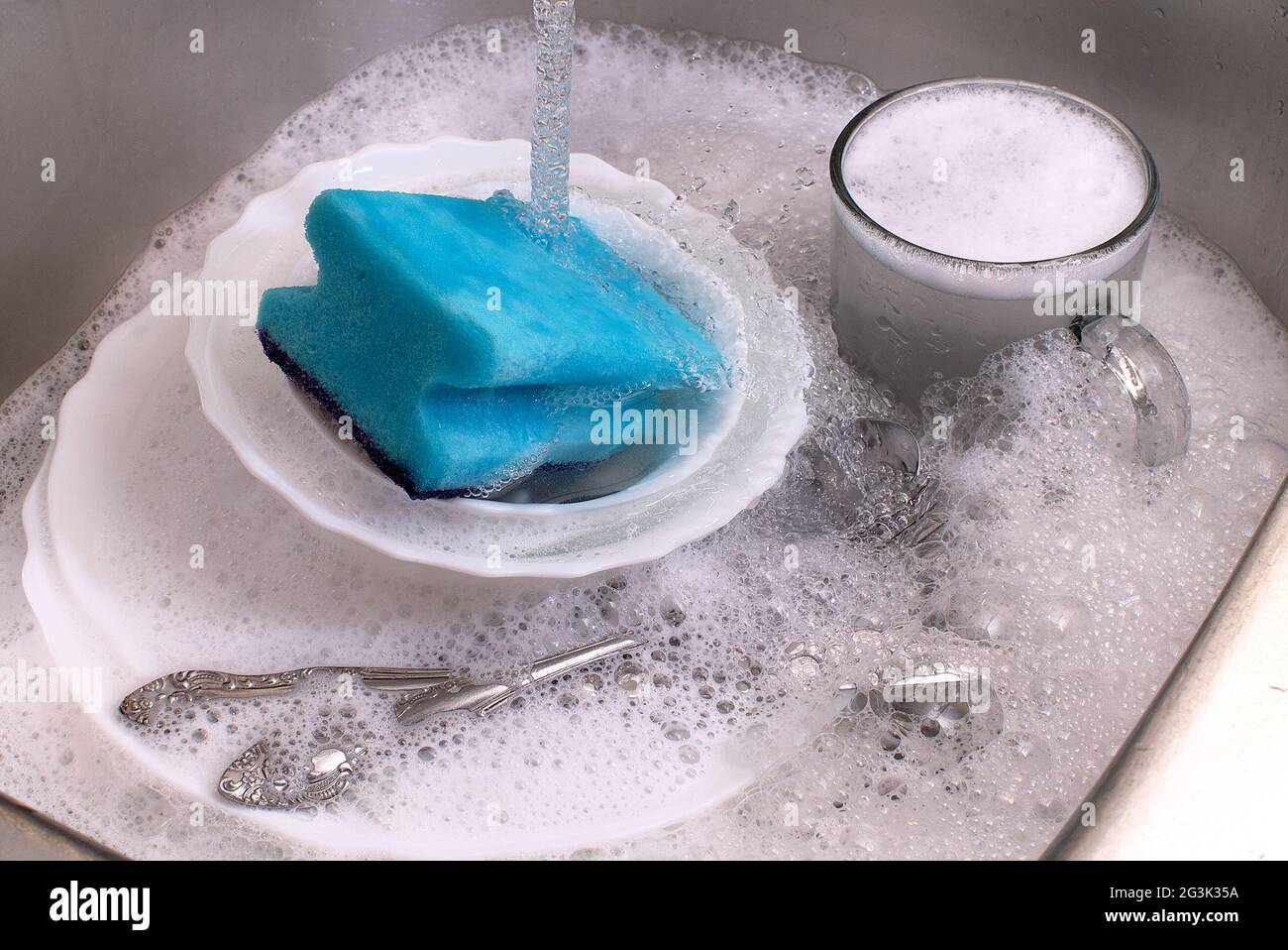 dirty dishware and utensils in kitchen sink with soap foam under ...