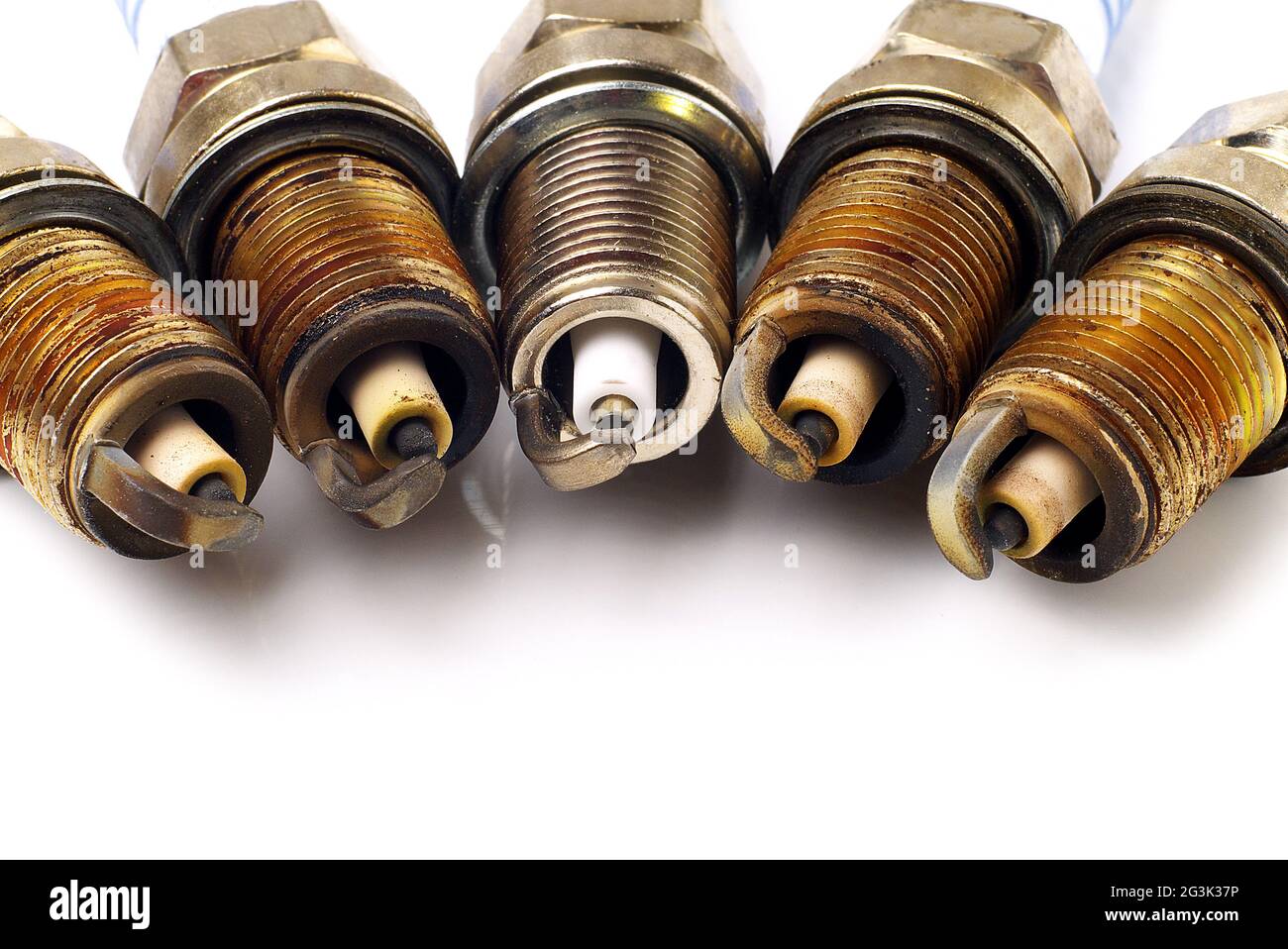 one brand new spark plug between four used ones on white background ...