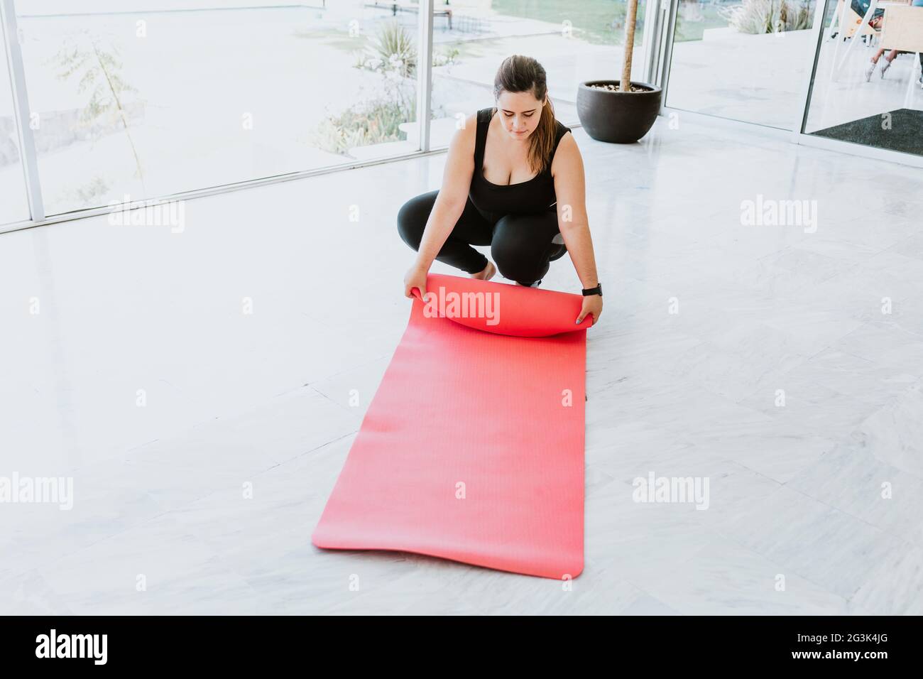 Latin girl unrolling yoga mat on the floor near the window at home ...