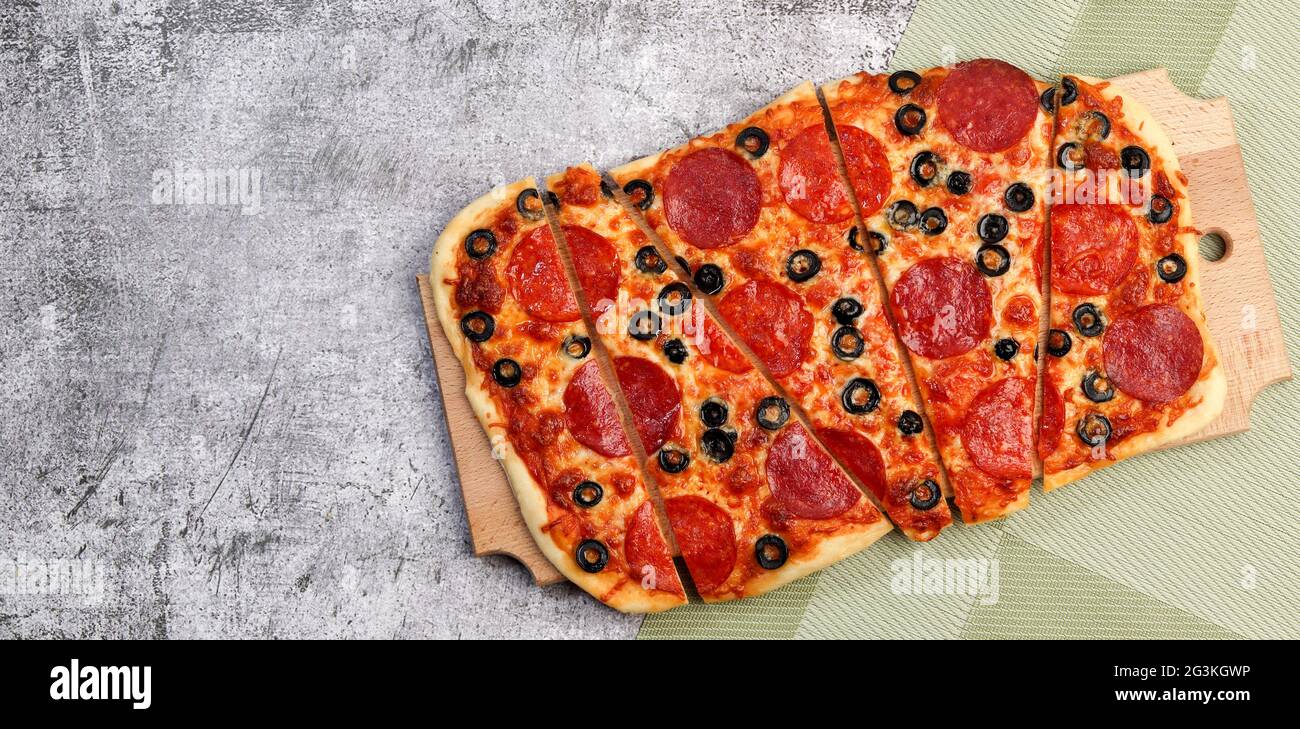 Sliced Rectangular pizza with pepperoni, cheese and olives on a ...
