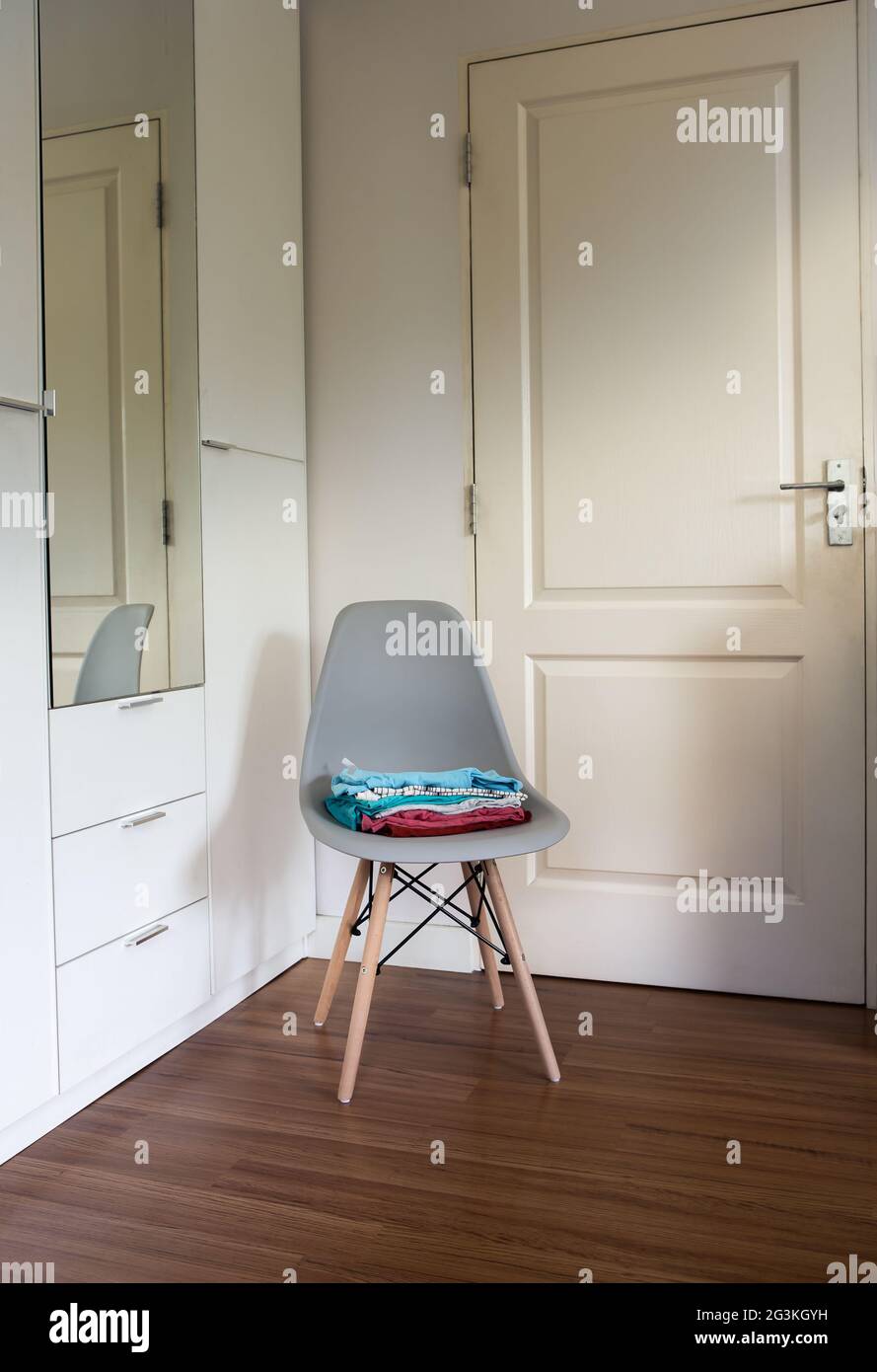 Stack of folded clean clothes on modern chair beside wardrobe in the ...