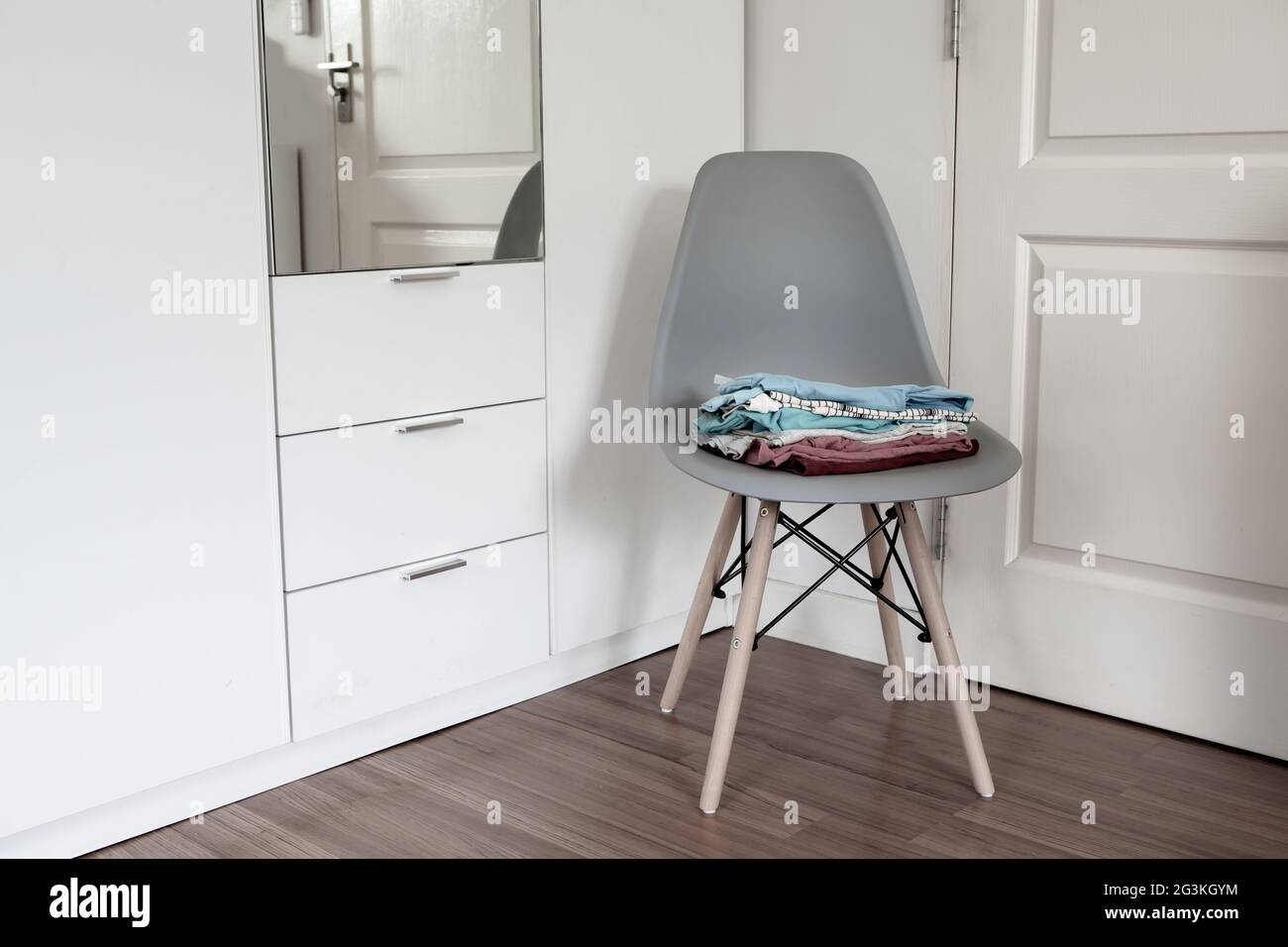 Stack of folded clean clothes on modern chair beside wardrobe in the ...