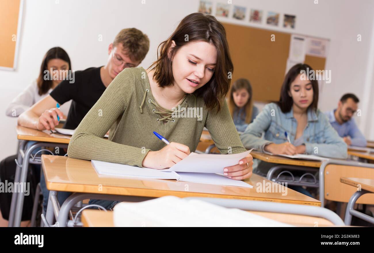 Young girl is writing test and thinking about questions at the desk ...