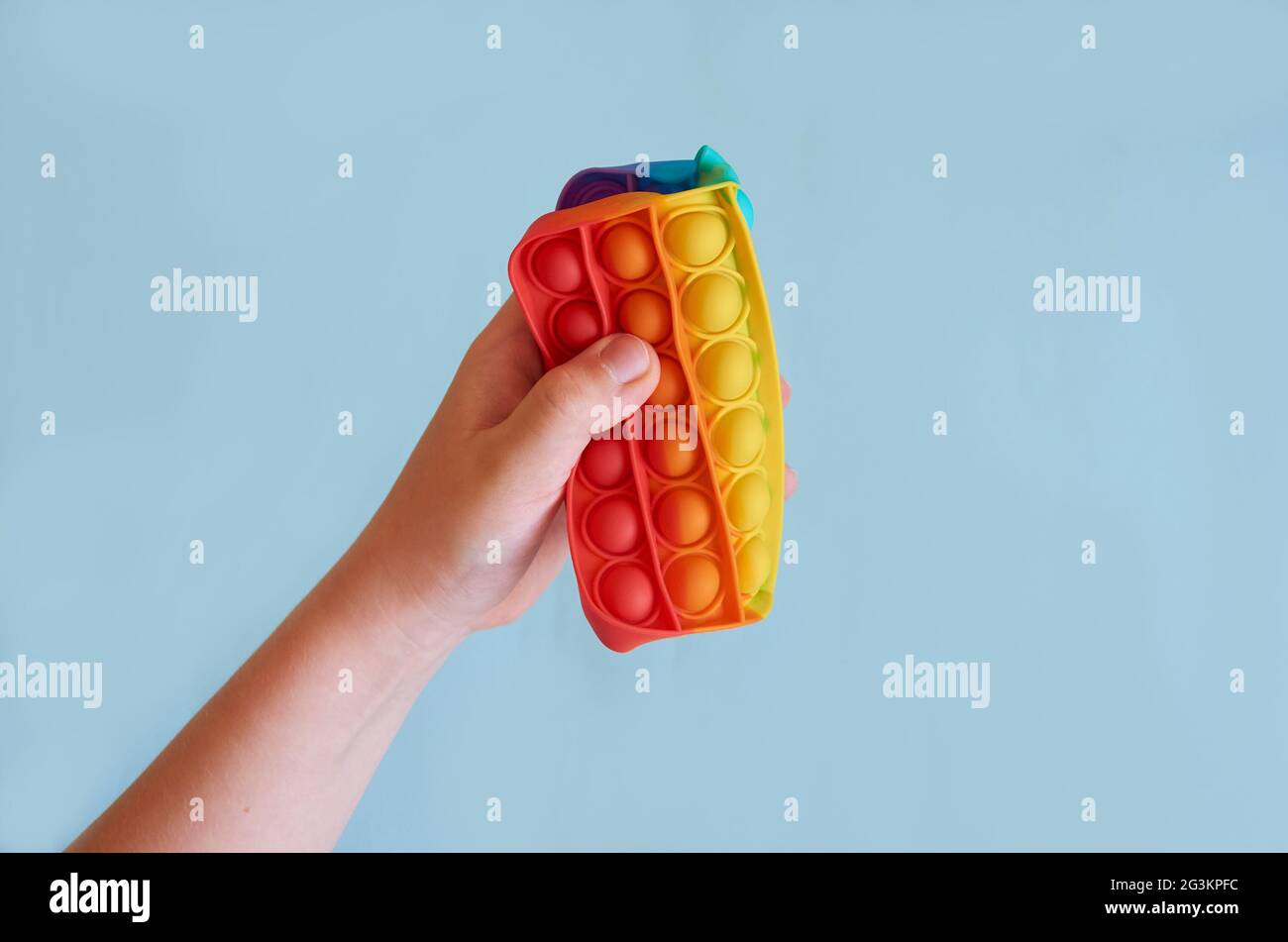 A child's hand squeezed in half a square silicone toy Pop It Stock ...