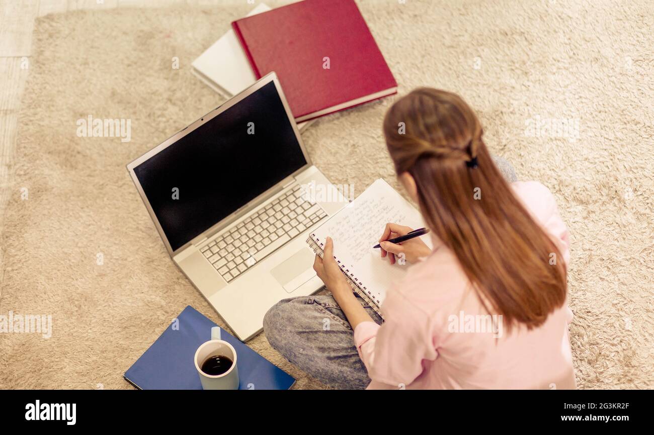 Top view of young girl sitting on carpet writing in notebook Stock ...