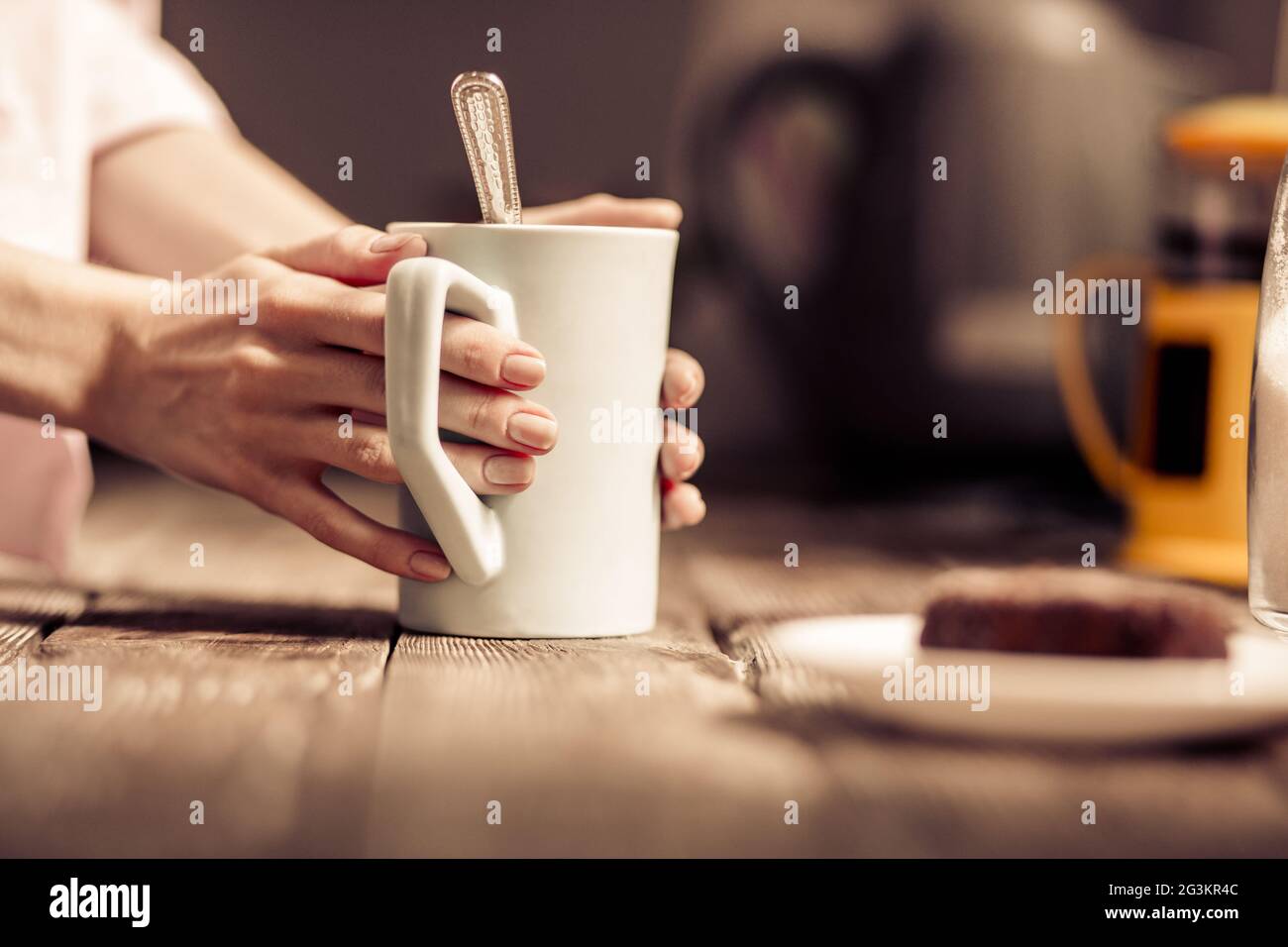 Female hands holding a white cup of tea standing close to wooden desk ...