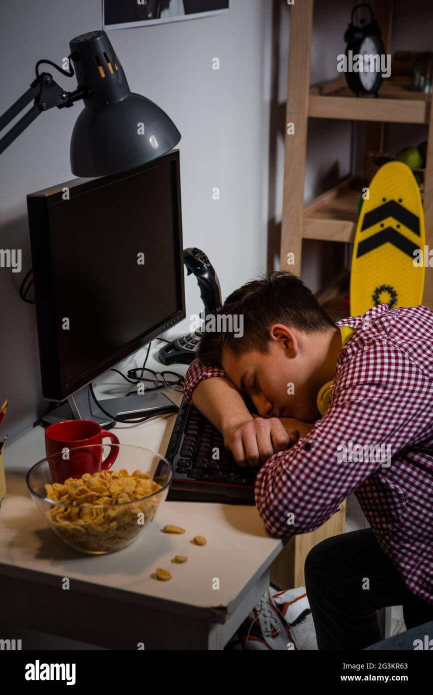 Teenage boy tired falling asleep at computer table Stock Photo - Alamy