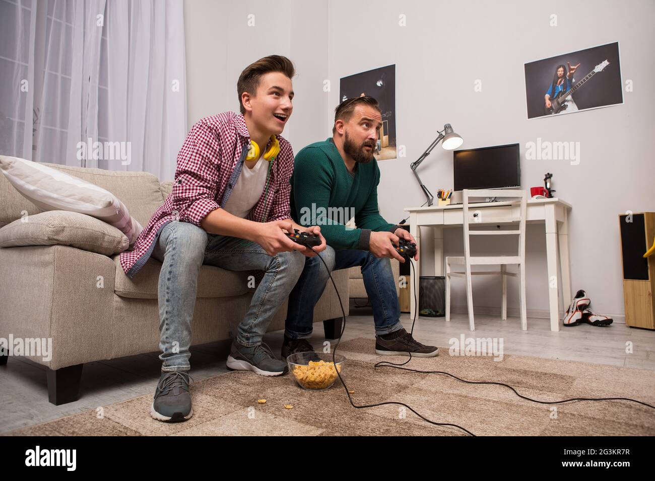 Side view of father and teenage son sitting on sofa, playing video ...