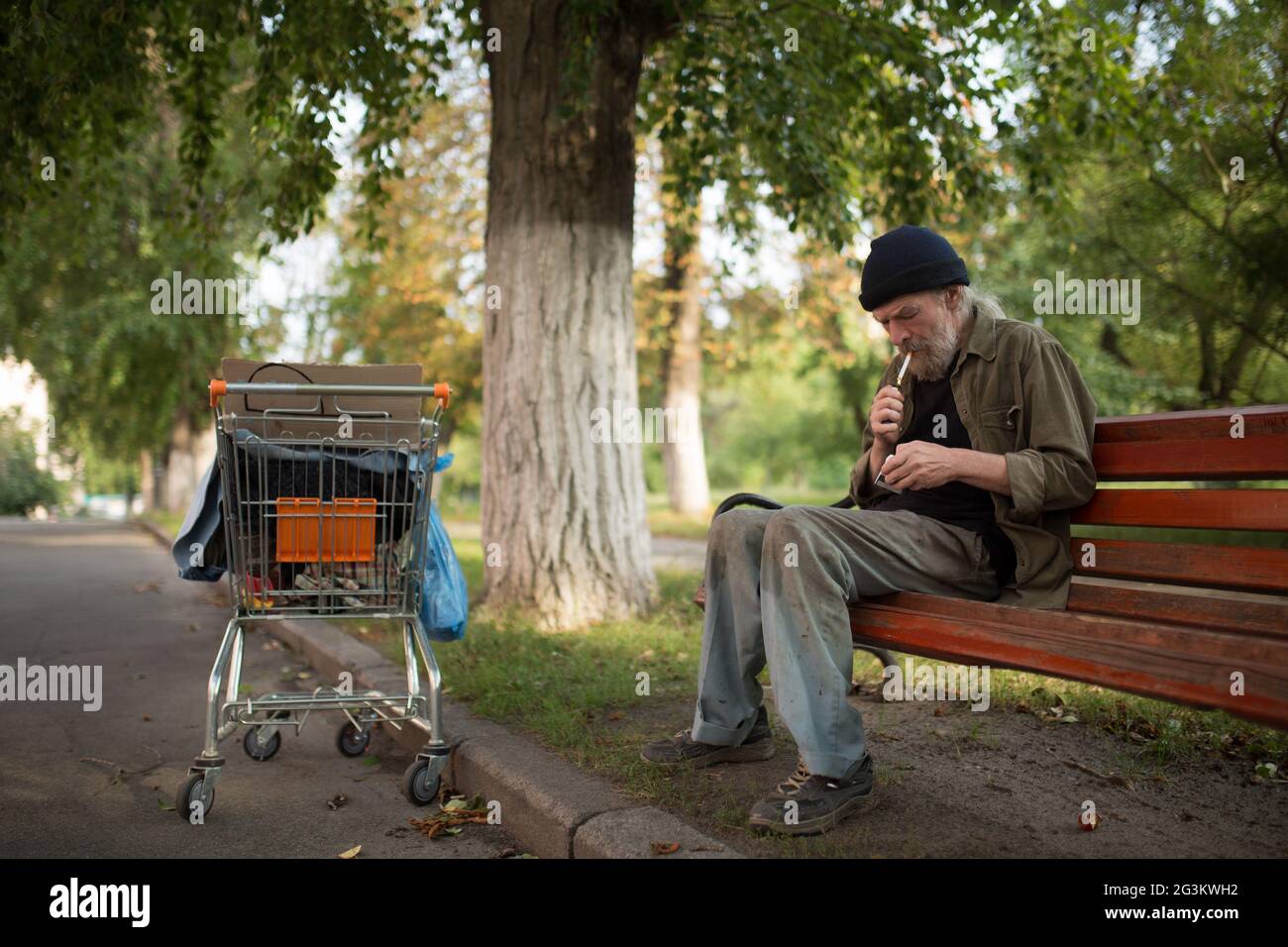 Homeless man sitting on bench lightning cigarette Stock Photo - Alamy